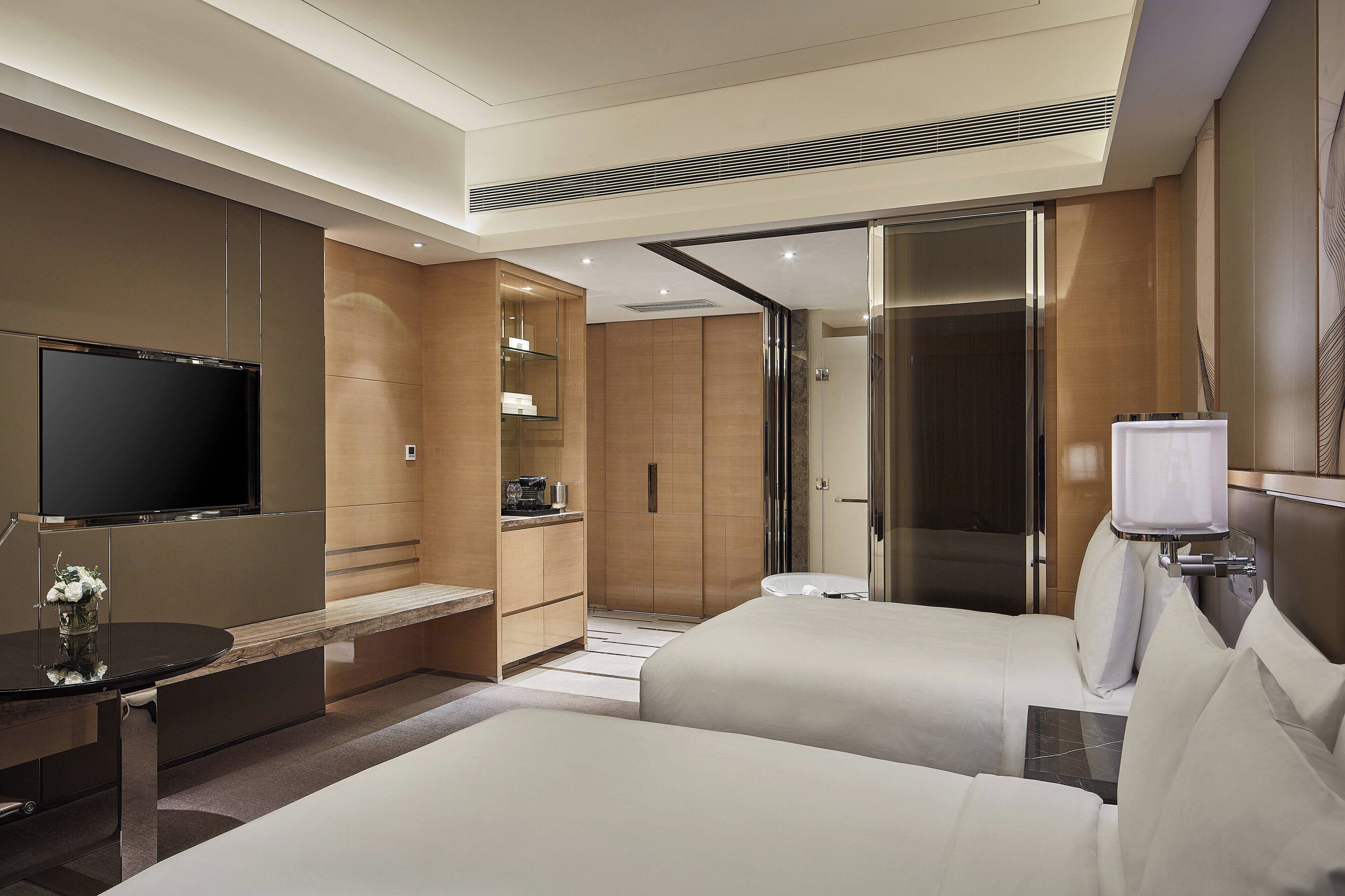 Quarto de hotel moderno com televisão de tela plana, escrivaninha com cadeira, duas camas, closet espaçoso e área de chuveiro.