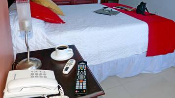 Quarto de hotel com cama, mesa de cabeceira, luminária, telefone, controle remoto e uma xícara de café.