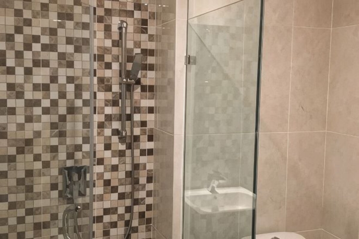 Um chuveiro com porta de vidro, parede revestida de azulejos e box de vidro.