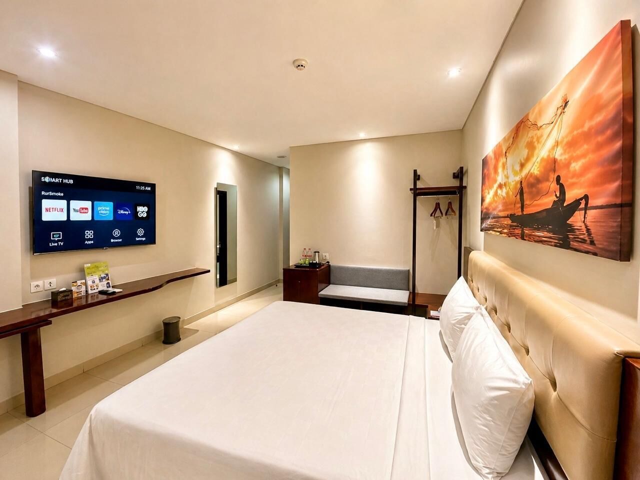 Quarto de hotel com cama, televisão exibindo serviços de streaming, um quadro na parede e um banco.