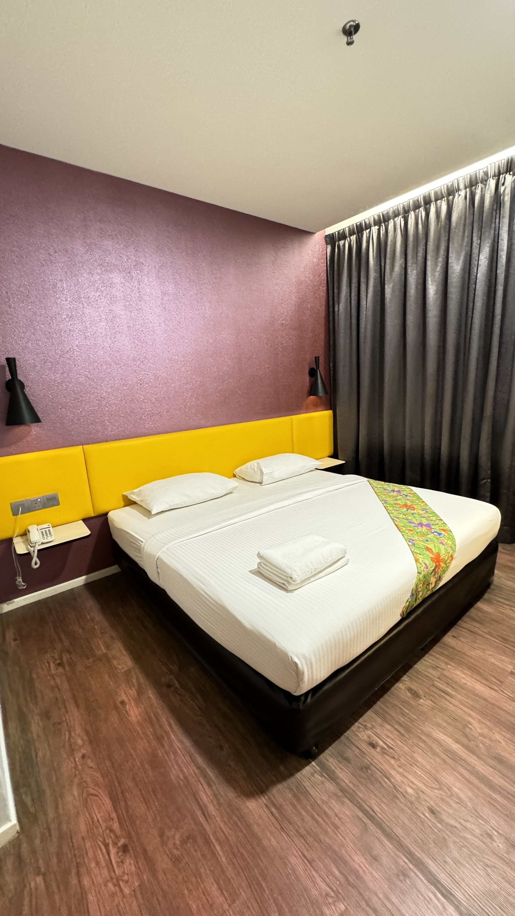 Quarto de hotel com uma cama, um telefone e uma luminária na mesa de cabeceira.