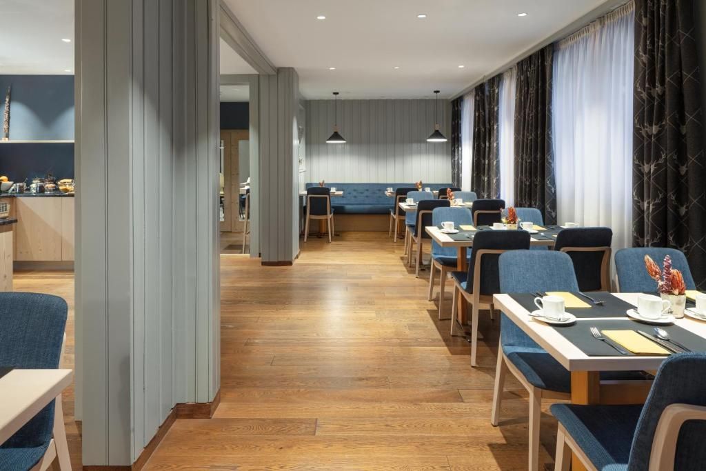 Uma área de refeições de hotel com várias mesas e cadeiras, um assento estofado azul e piso de madeira.