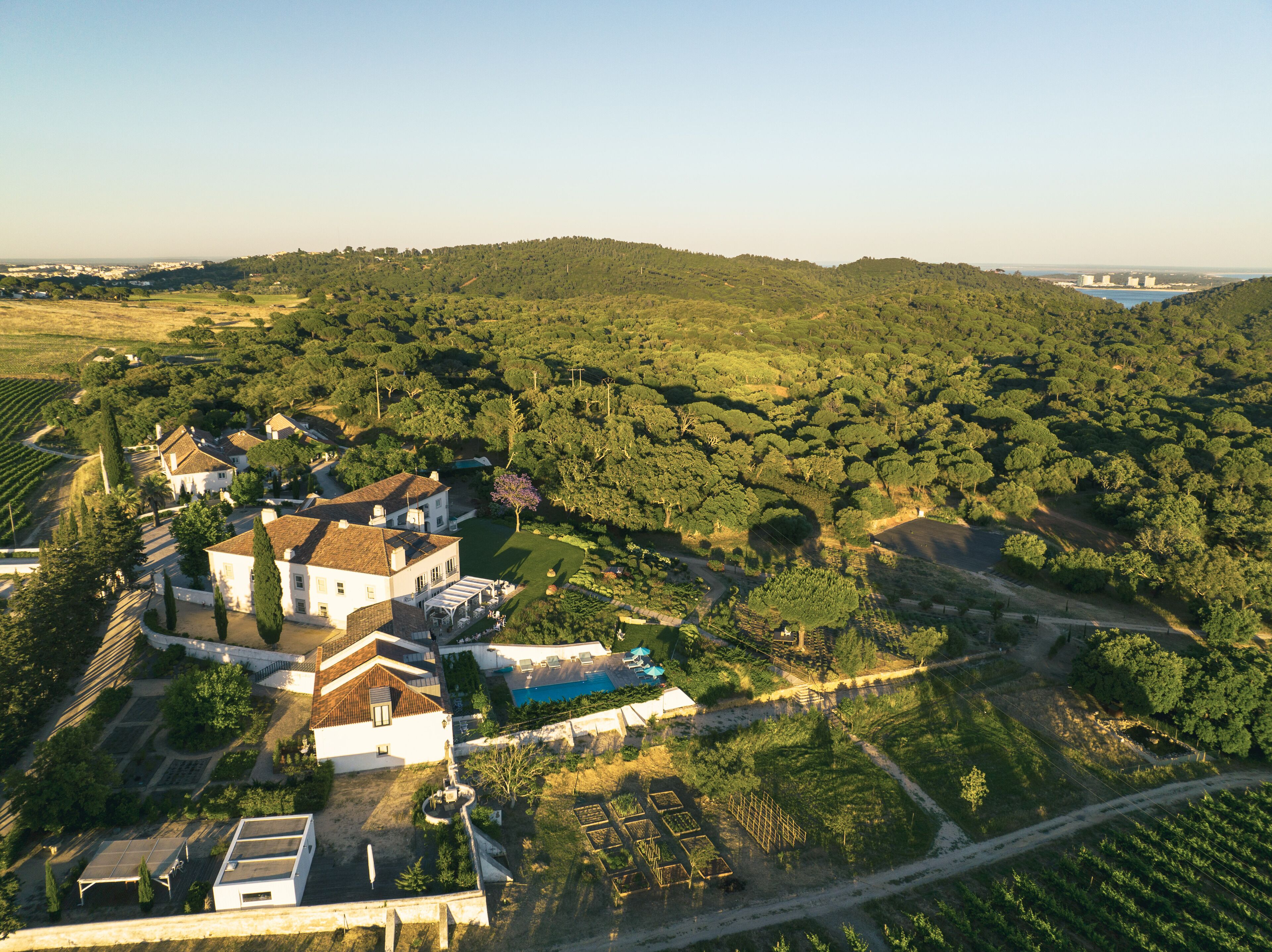 Vista aérea de uma grande propriedade com vários edifícios, piscina e jardins extensos.