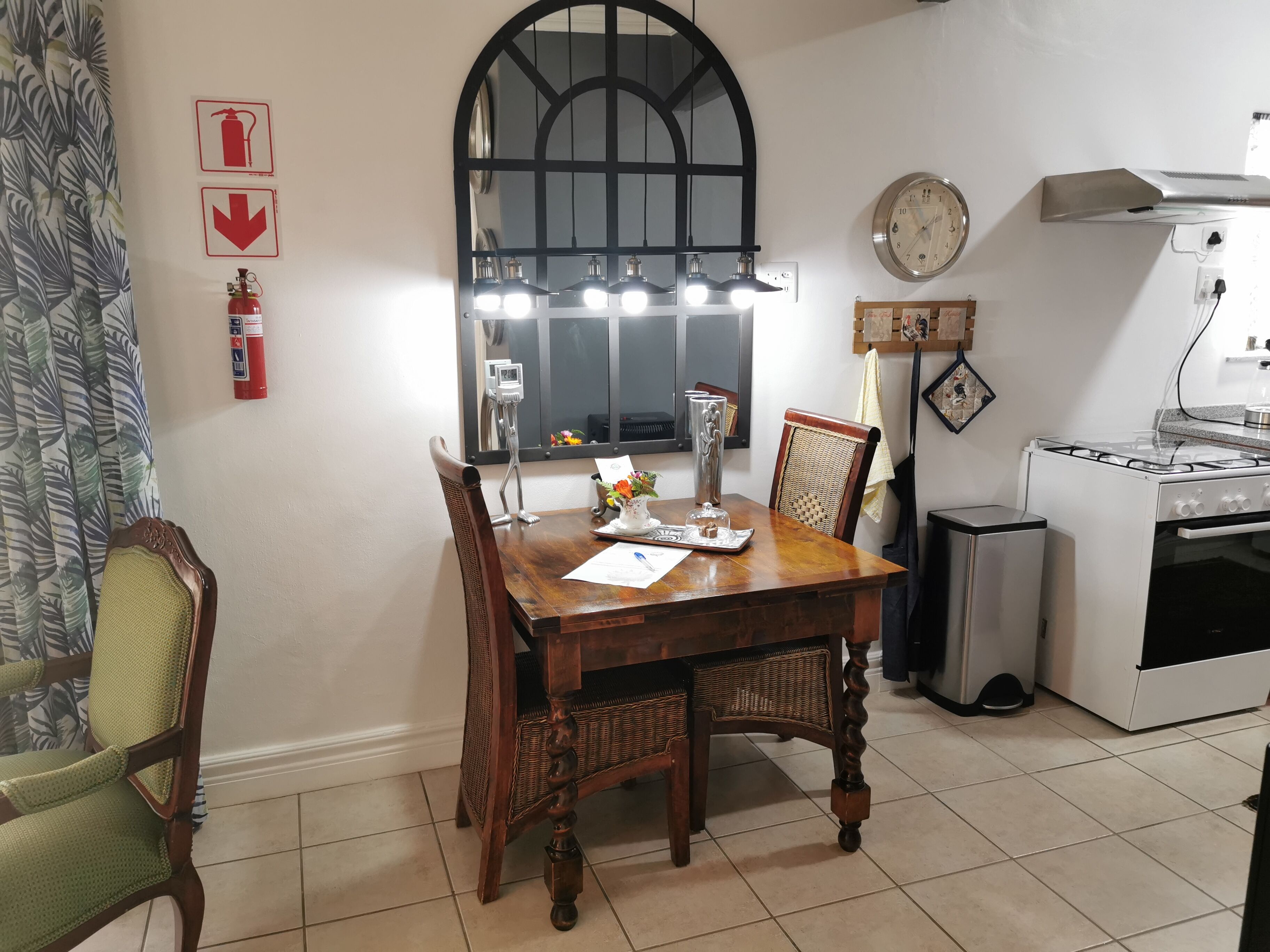 Uma área de refeições com mesa de madeira, cadeiras, espelho e extintor fixado na parede.