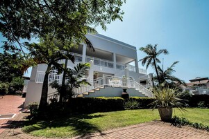 Um edifício de dois andares com fachada branca, uma varanda no andar superior e uma escadaria que leva à entrada.