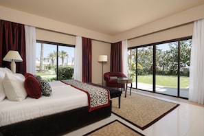 Quarto de hotel espaçoso com uma cama grande, área de estar com uma poltrona e mesa, e janelas amplas com vista para o exterior.