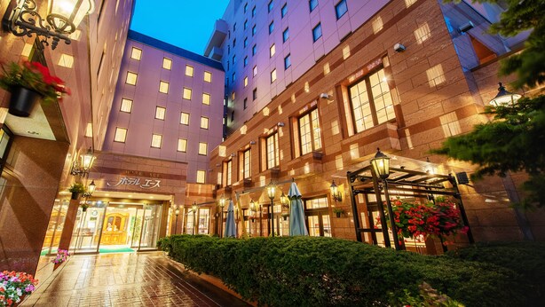 Entrada de hotel com fachada bem iluminada, área de estar coberta ao ar livre e um caminho que leva à entrada.