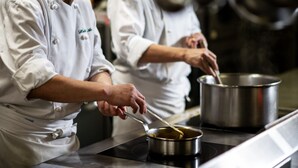Cozinheiros de uniformes brancos preparando alimentos em uma cozinha profissional.
