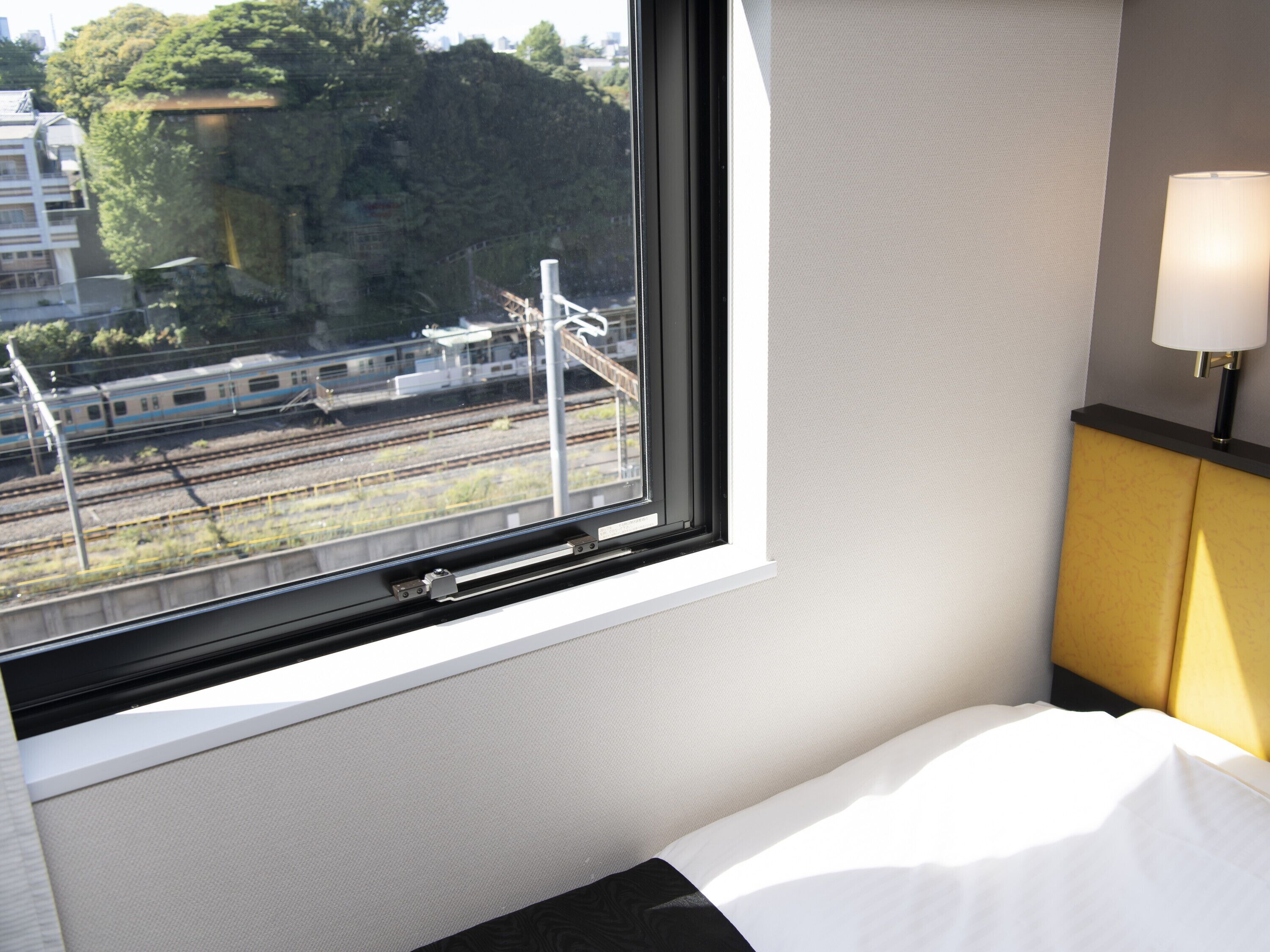Quarto de hotel com janela que dá para uma linha férrea e uma paisagem montanhosa.