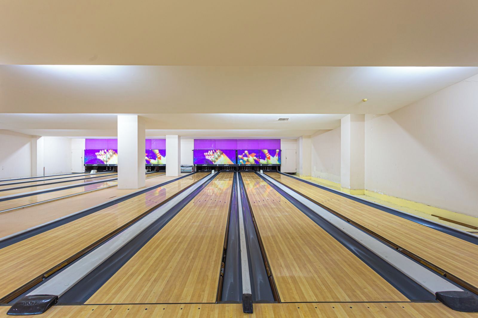 Uma pista de boliche com várias pistas, piso de madeira e iluminação roxa ao fundo.