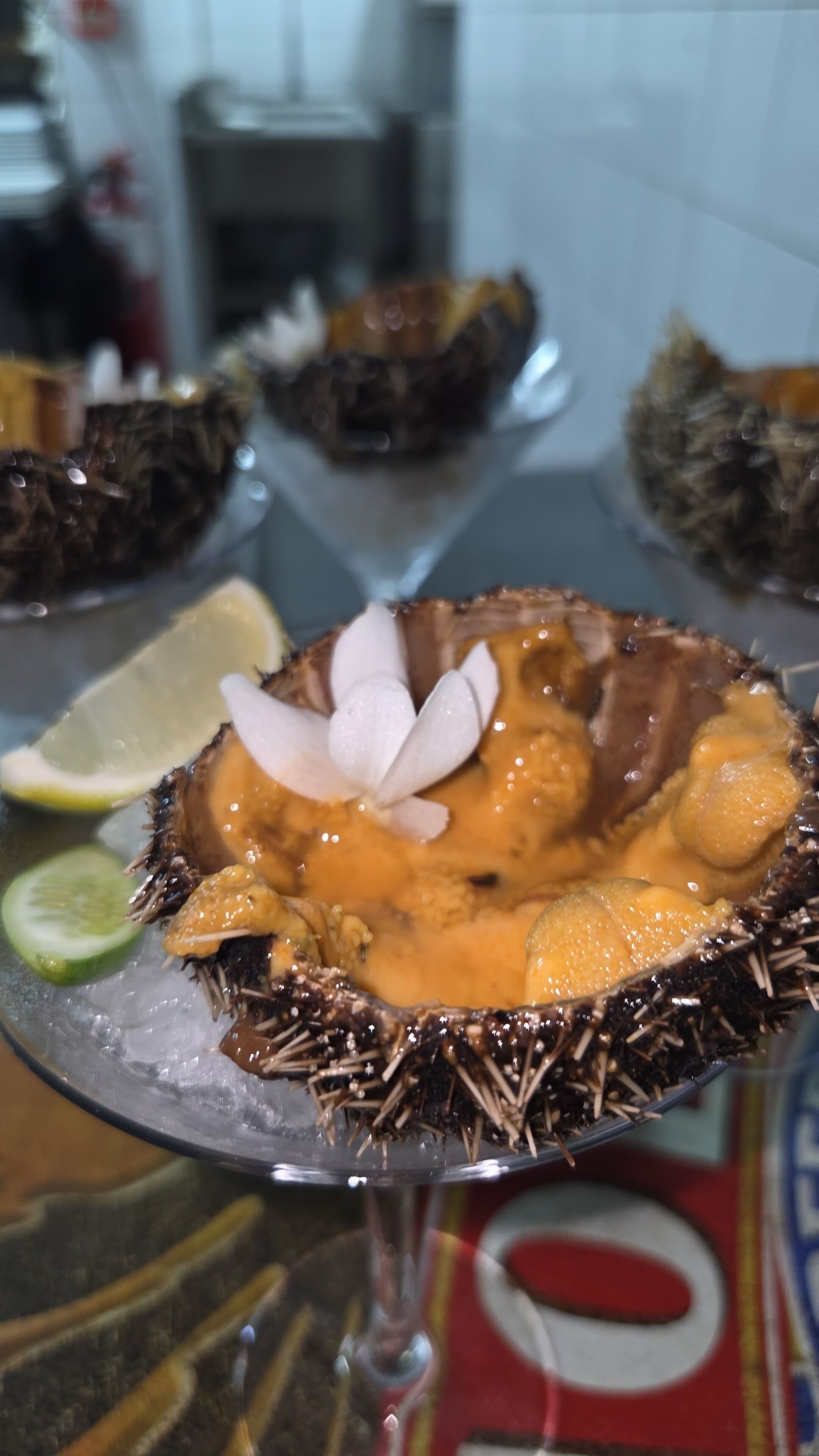 Prato de marisco com casca, guarnecido com rodelas de cebola, servido numa travessa de vidro com gelo.
