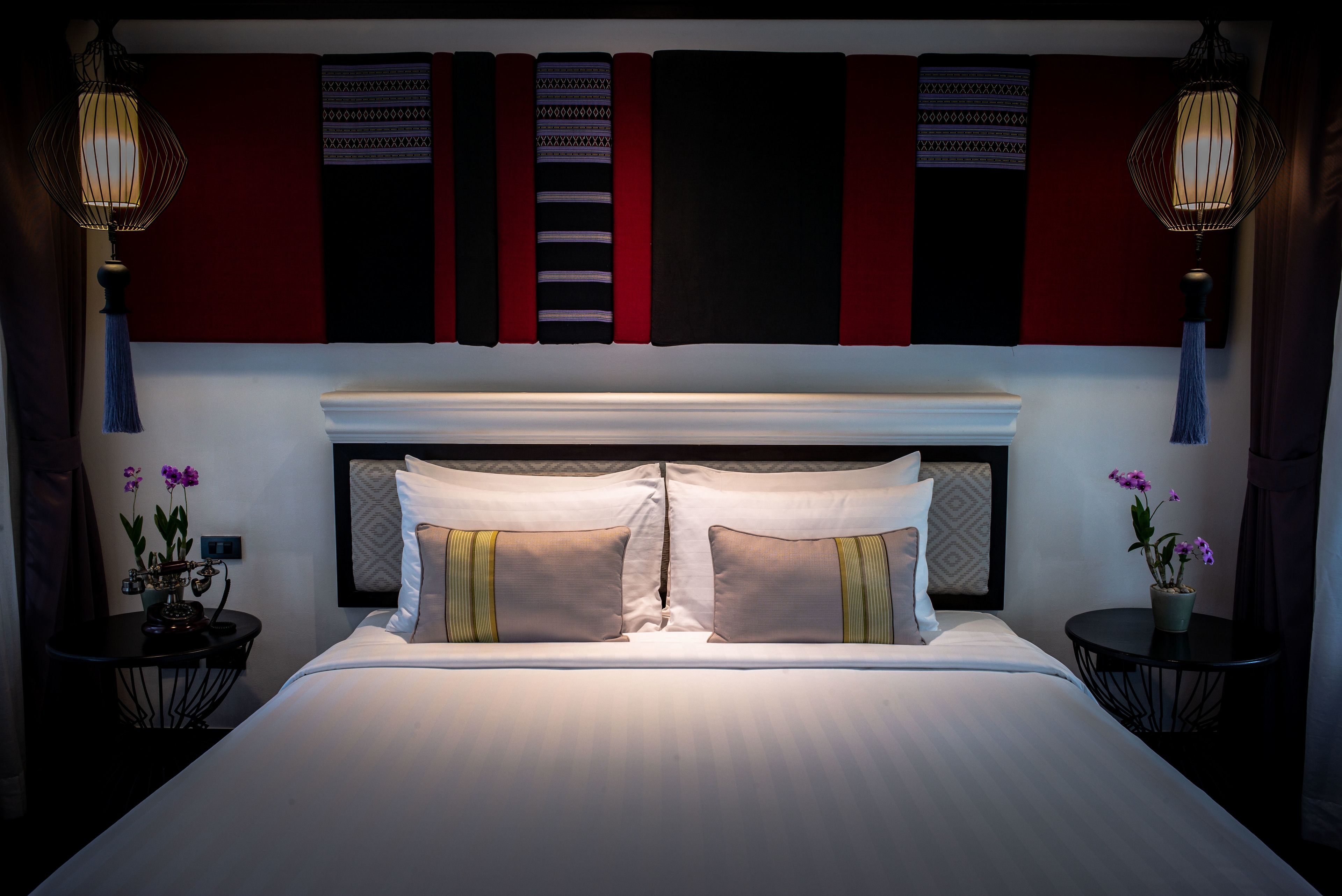 Cama bem arrumada com lençóis brancos e duas almofadas, com dois mesinhas de cabeceira com luminárias e pequenas mesas.