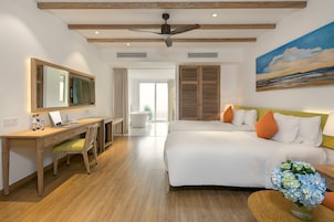 Quarto de hotel moderno com escrivaninha de madeira, cama com roupa de cama branca, espelho grande e uma pintura do pôr do sol.