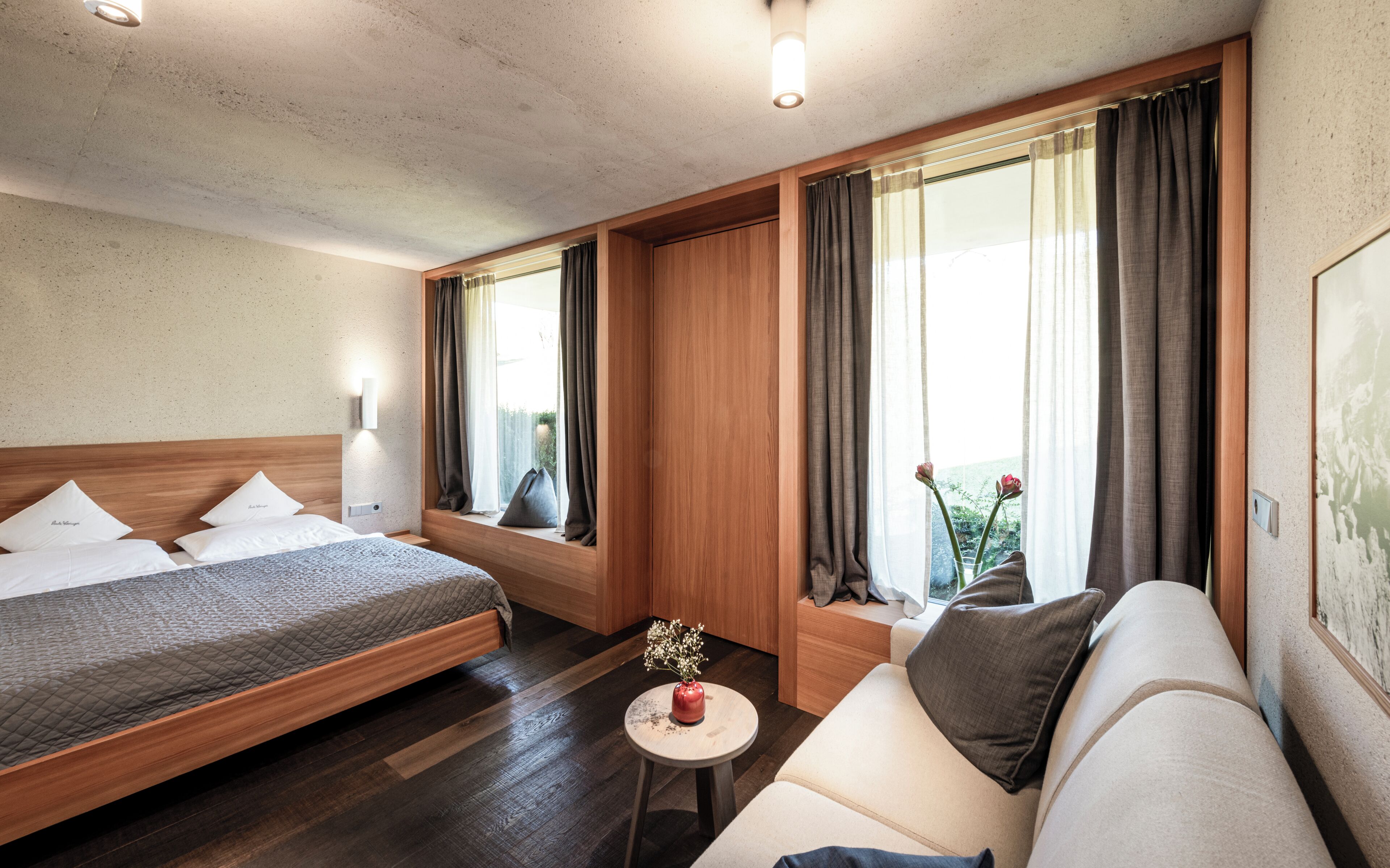 Quarto de hotel com cama, sofá, uma pequena mesa e janela com cortinas.