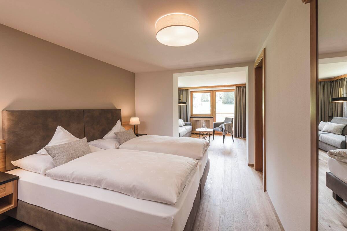 Quarto de hotel com duas camas, uma mesinha de cabeceira, abajur, janela e vista para o exterior.