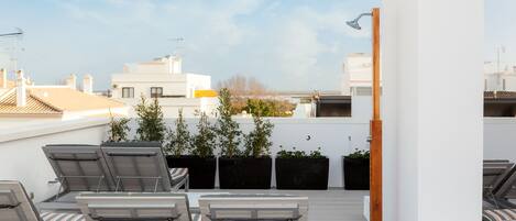 Terraço no telhado com cadeiras de descanso, plantas em vasos e vista para a cidade.