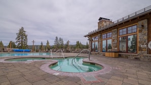 Área de piscina com hidromassagem, espreguiçadeiras e um edifício com grandes janelas.