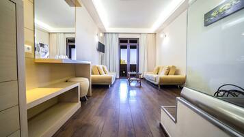 Uma sala de estar moderna com um sofá, uma mesinha e uma televisão. Há uma porta que dá para outro quarto.