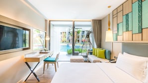 Quarto de hotel com cama, escrivaninha, cadeira e vista para uma piscina e edifícios.