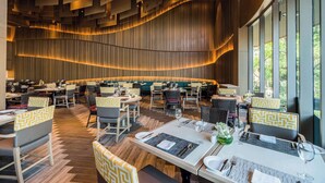 Um restaurante amplo com várias mesas e cadeiras, com design moderno e padrões geométricos nos móveis e teto de madeira.