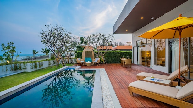 Uma área de piscina moderna ao ar livre com deck de madeira, cadeiras de descanso e um guarda-sol amarelo.