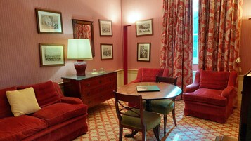 Um quarto com um sofá vermelho, uma mesa de madeira, cadeiras, uma cômoda e quadros nas paredes.