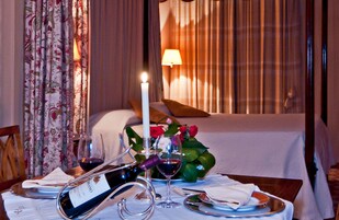 Quarto de hotel com uma mesa de jantar bem posta, uma vela acesa e um buquê de rosas.