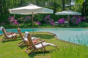 Uma área de piscina com espreguiçadeiras e guarda-sóis, cercada por vegetação exuberante e plantas floridas.