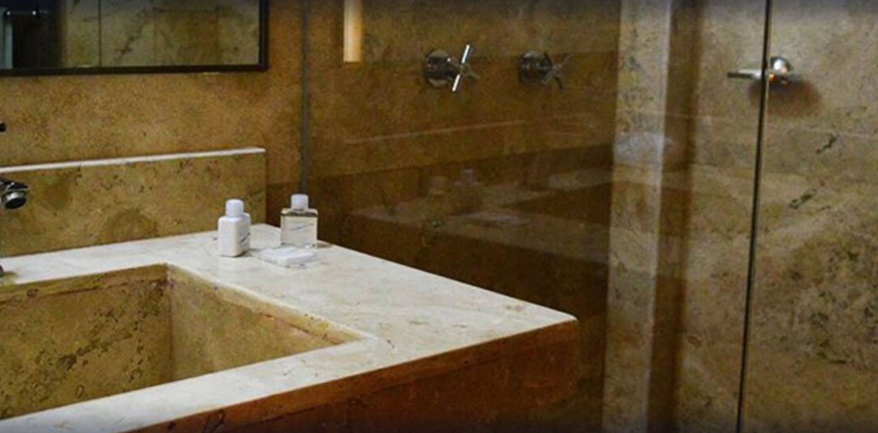 Casa de banho com lavatório de mármore, espelho e cabine de duche em vidro.