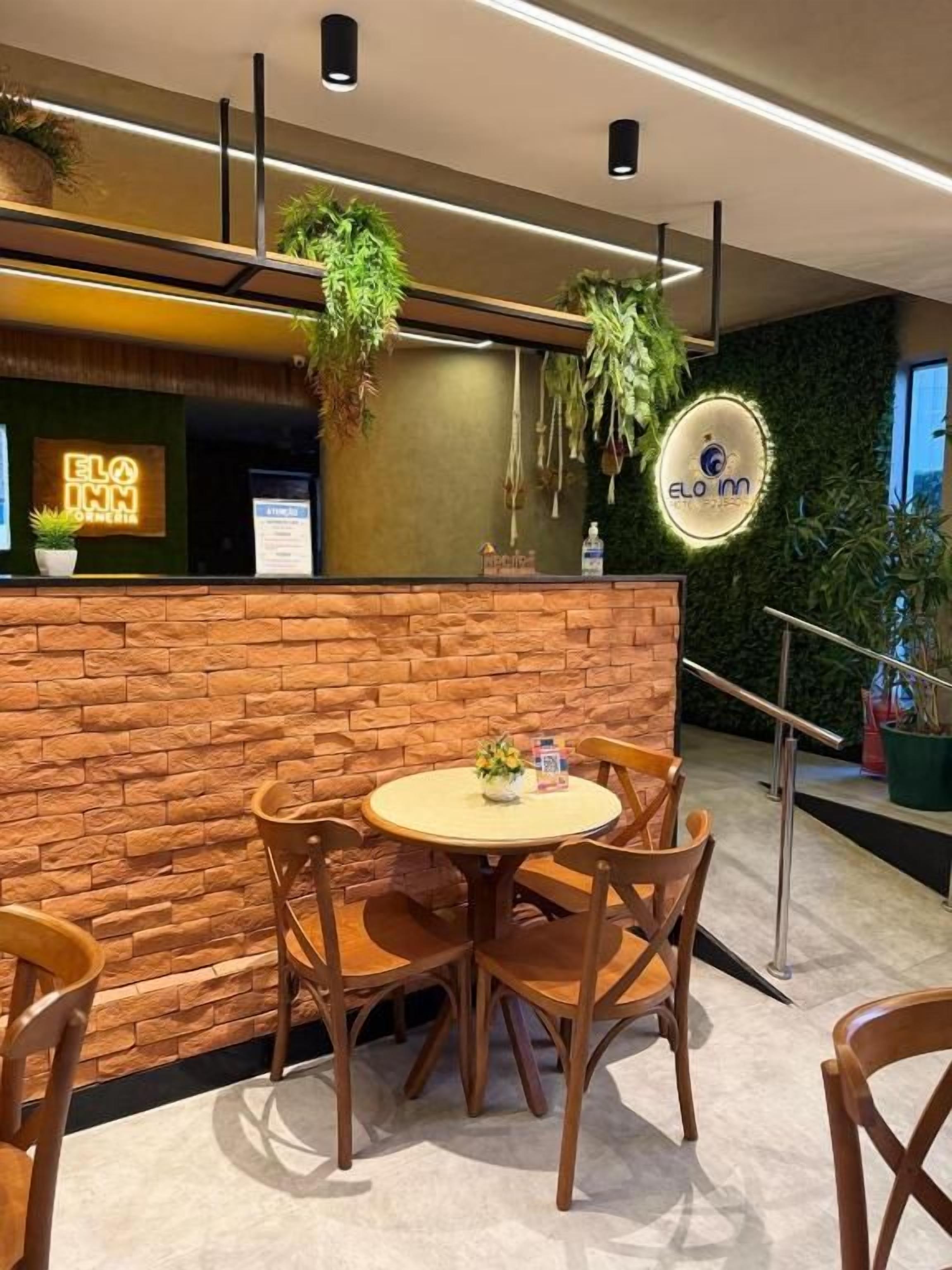 Uma área de recepção com parede de tijolos, uma mesa redonda com cadeiras e um letreiro de neon.