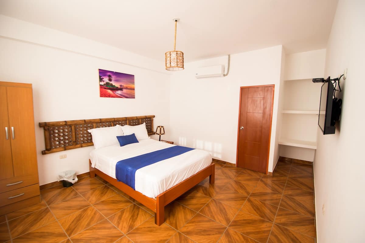 Quarto bem arrumado com cama de madeira, cabeceira, um quadro, luminária pendente e guarda-roupa.