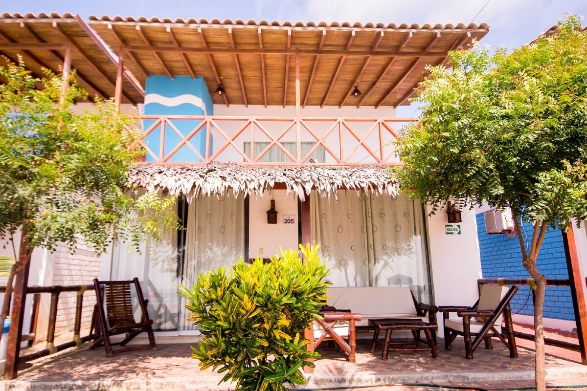 Uma área de estar externa com mesa e cadeiras, um telhado de palha e uma parede azul com um design de ondas.