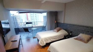 Quarto de hotel com duas camas, uma escrivaninha com cadeira e vista para a cidade.