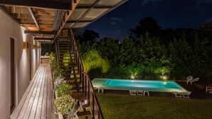 Um deck de madeira com piscina, área de estar ao ar livre e escadaria para uma área coberta.