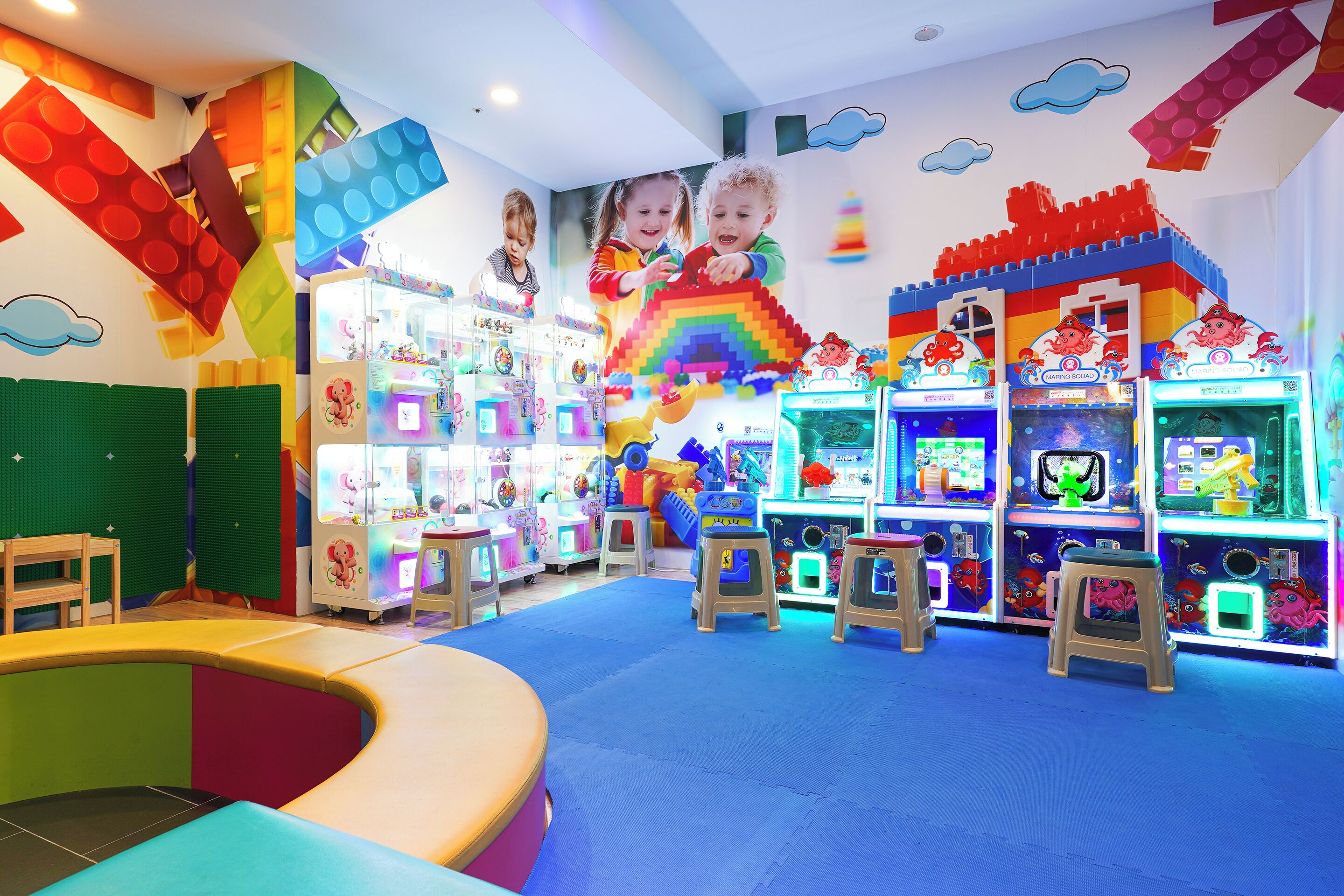 Uma área de recreação interna bem iluminada, com estruturas coloridas, jogos de fliperama e uma pequena piscina.