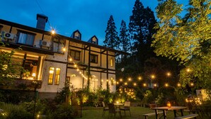 Um edifício de dois andares com varanda, luzes de festa e área de estar externa.