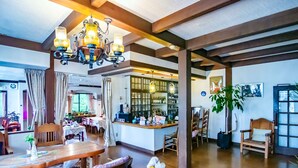 Uma ampla sala de jantar com uma mesa e cadeiras de madeira, um candelabro e um espaço de bar com prateleiras cheias de garrafas.