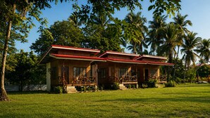Uma casa de dois andares com telhado vermelho, cercada por um gramado bem cuidado e palmeiras.