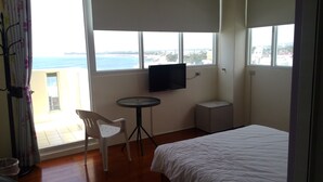 Quarto de hotel com uma cama, uma mesa pequena, uma cadeira, uma televisão e uma janela com vista para o mar.