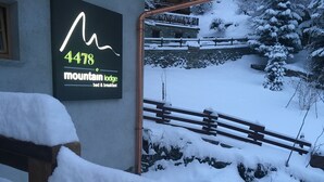 Placa de Mountain Lodge com serviço de hospedagem e café da manhã, emoldurada por uma paisagem coberta de neve e construções de madeira.