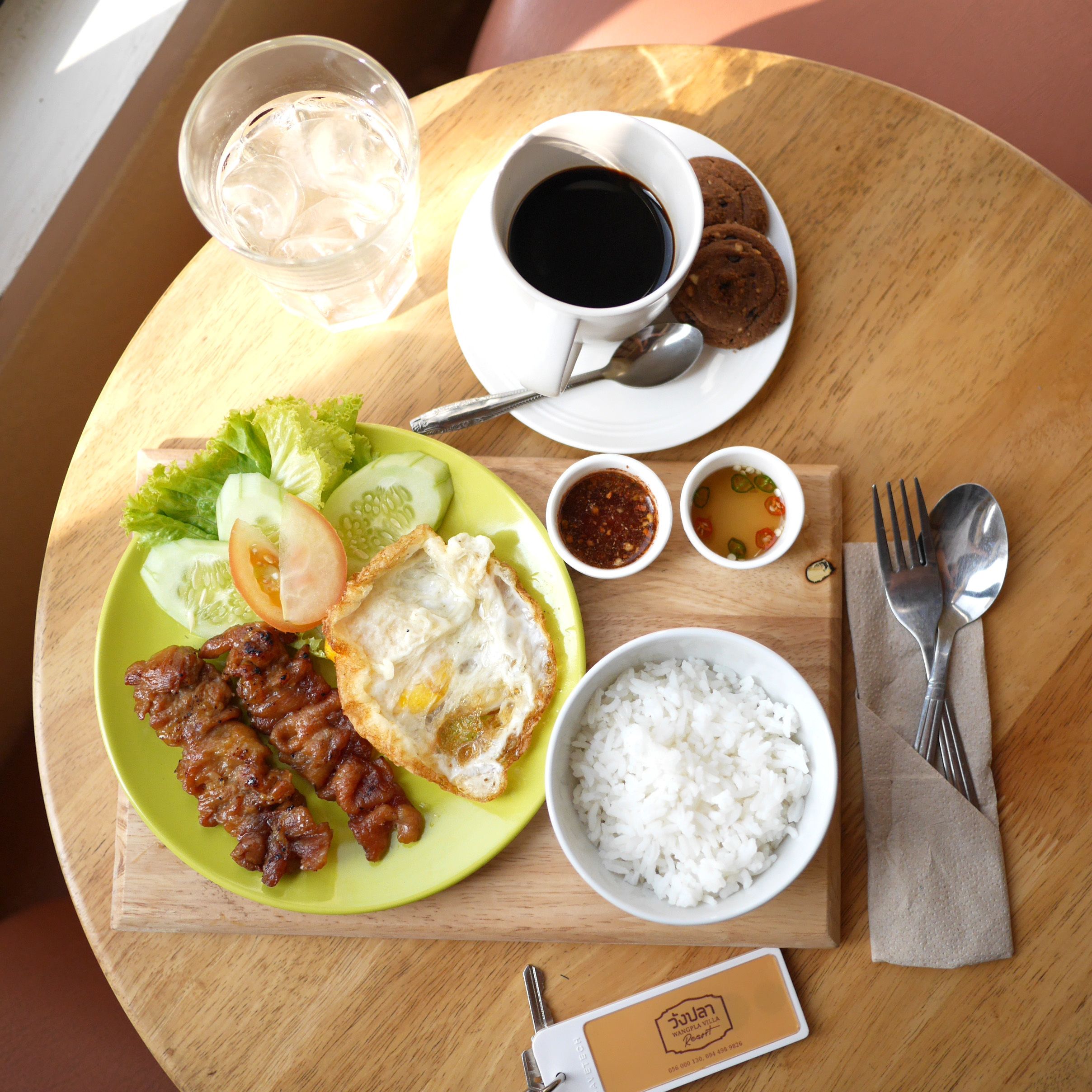 Prato com carne grelhada, ovo frito, arroz e legumes sobre uma mesa de madeira.