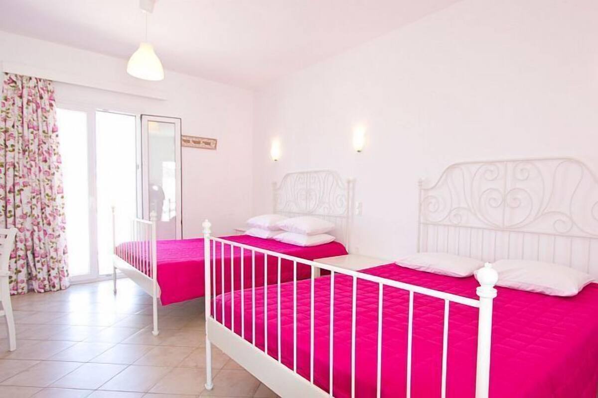 Quarto com duas camas, cabeceiras de metal branco e esquema de cores claras e brancas.