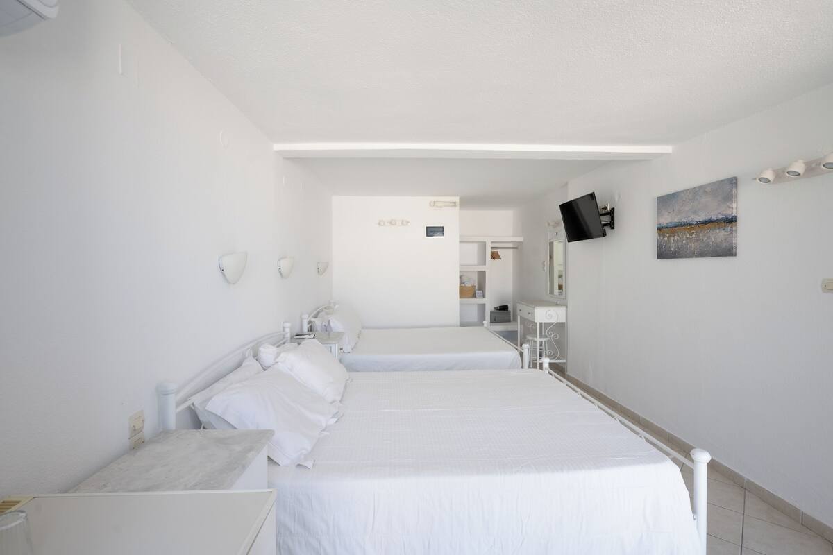 Quarto de hotel com duas camas, uma escrivaninha, uma cadeira, televisão na parede e um quadro.