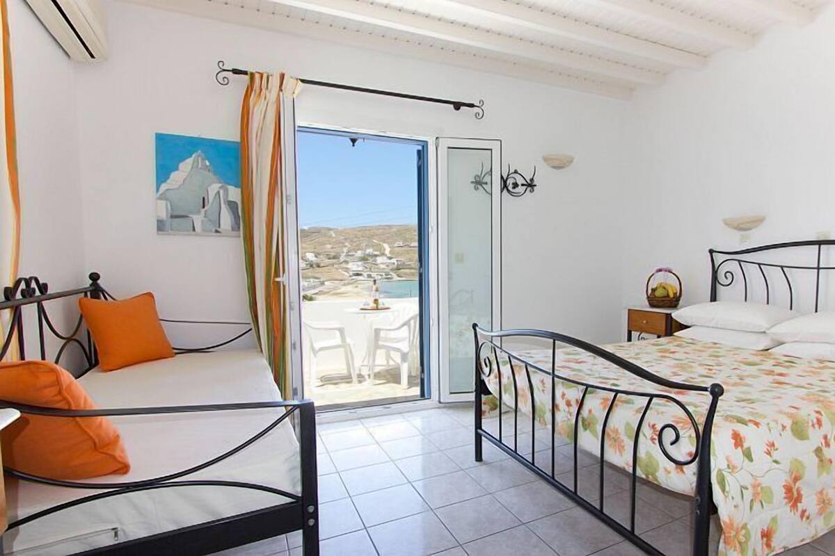 Quarto com cama, uma cadeira, uma mesinha e vista para o exterior.