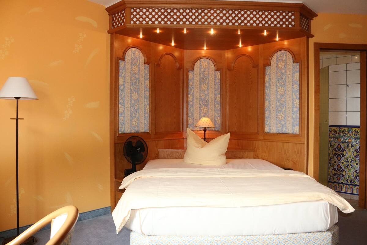 Quarto com cama de dossel, luminária de chão e ventilador.