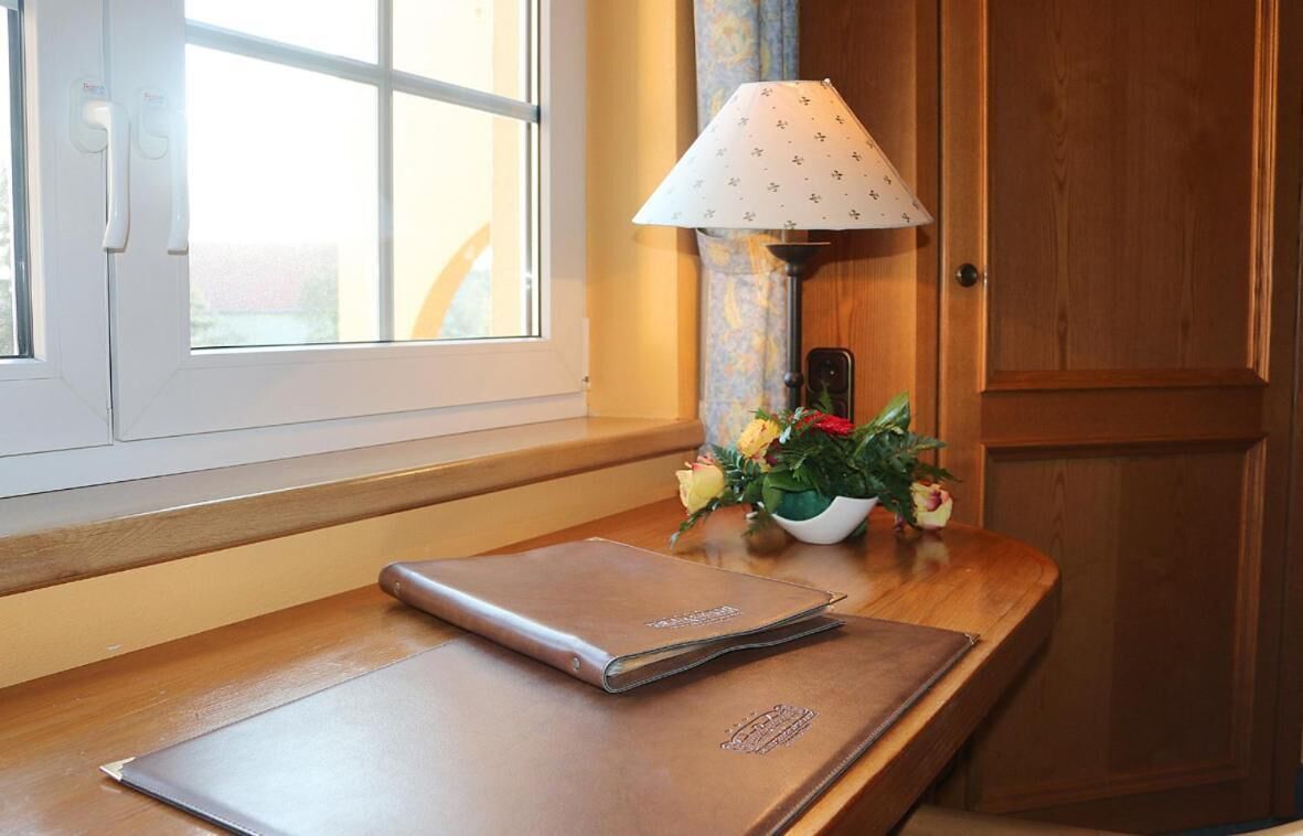 Uma secretária de madeira com um laptop, uma luminária e um vaso de flores.