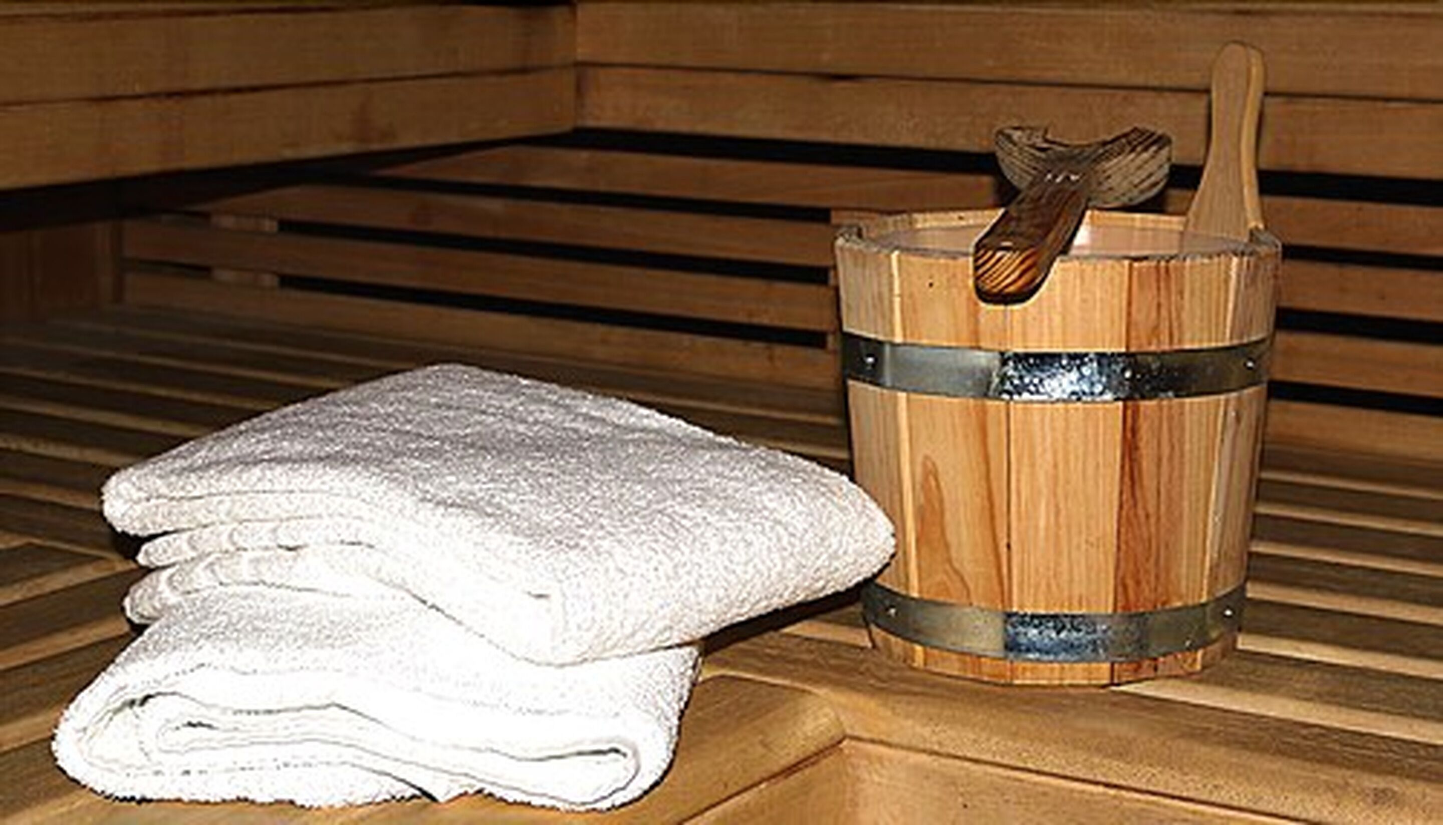 Um banco de sauna de madeira com uma toalha e um balde de madeira com uma concha.