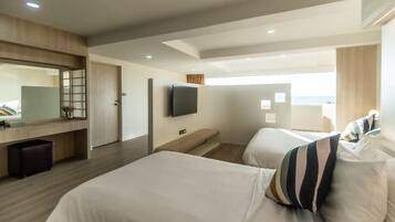 Quarto de hotel moderno com duas camas, televisão, um espelho grande e vista para o mar.
