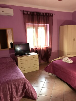 Quarto com duas camas, televisão em uma cômoda, armário e janela com cortinas.