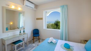 Quarto de hotel com cama, escrivaninha, uma cadeira, um espelho grande e janela com vista para o mar.